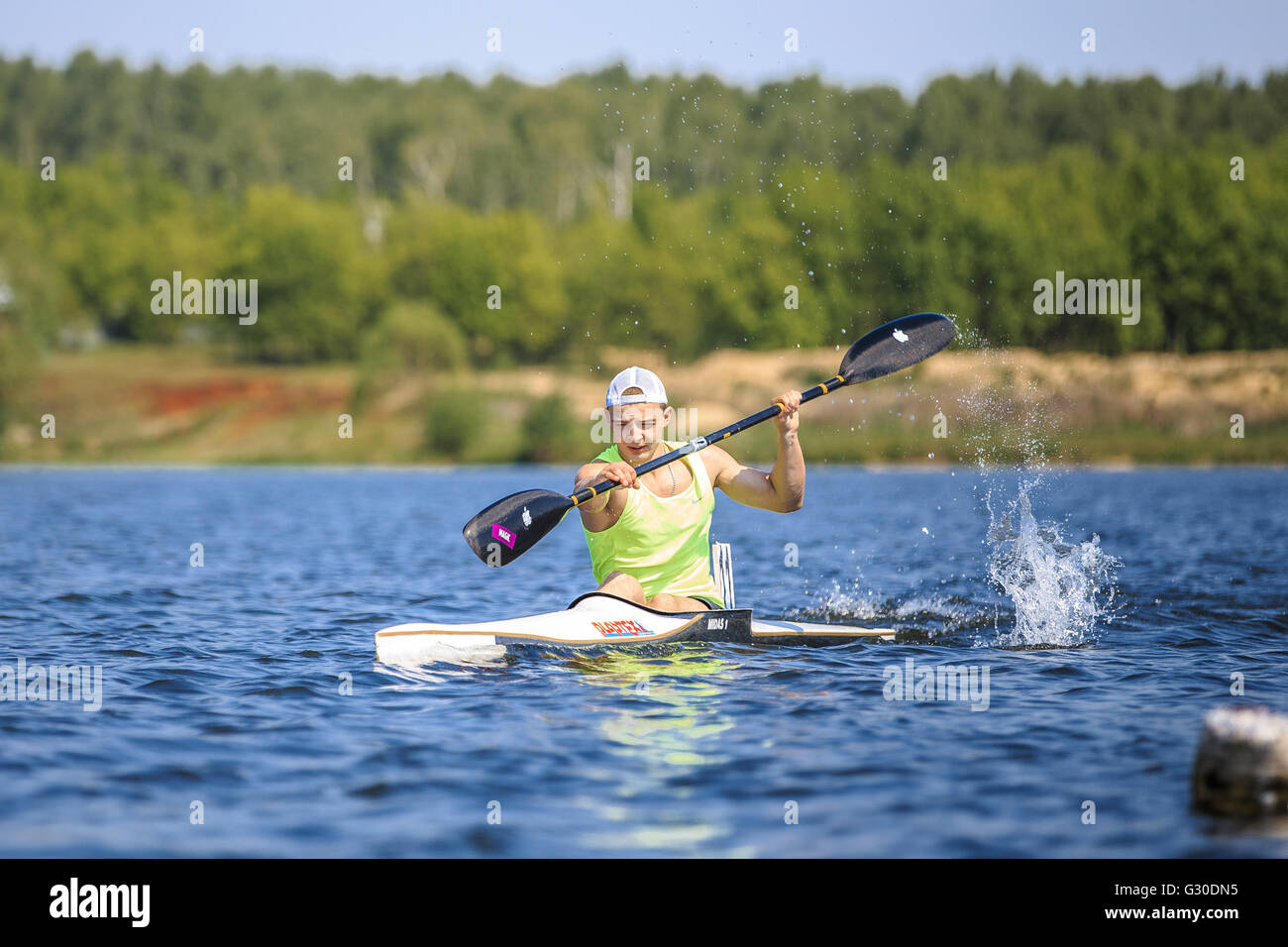 athlete at rowing kayak on lake, spray of water under paddle during ...