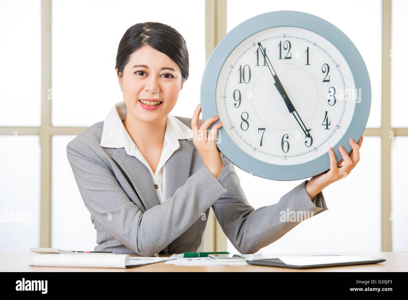 Happy business woman showing clock in office Stock Photo - Alamy