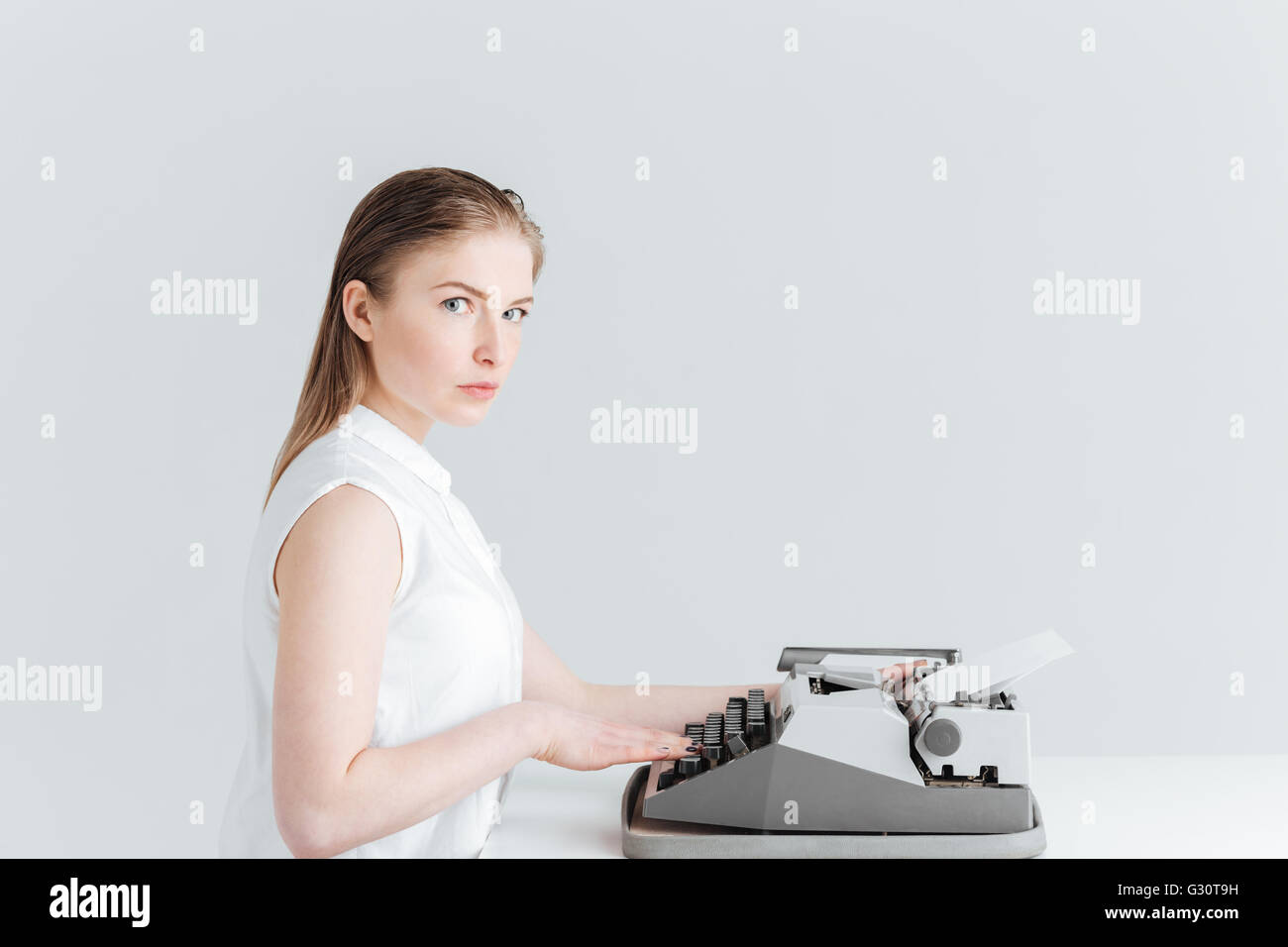 Young woman typing on retro machine and looking at camera isolated on a ...