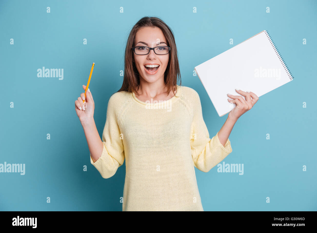 Laughing cheerful pretty girl holding notebook isolated on the blue ...