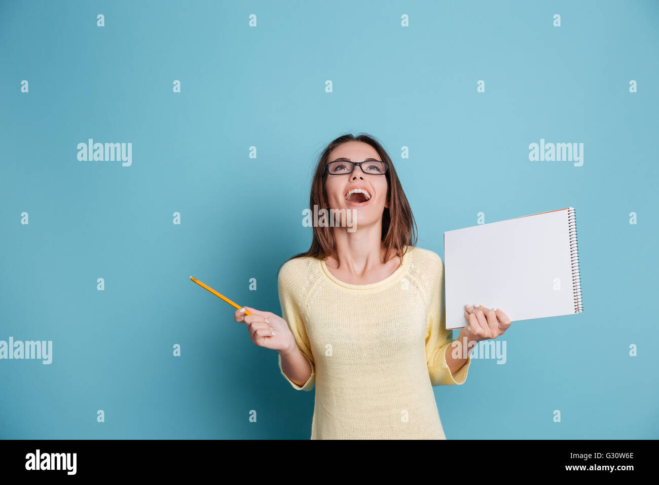 Laughing cheerful pretty girl holding notebook isolated on the blue ...