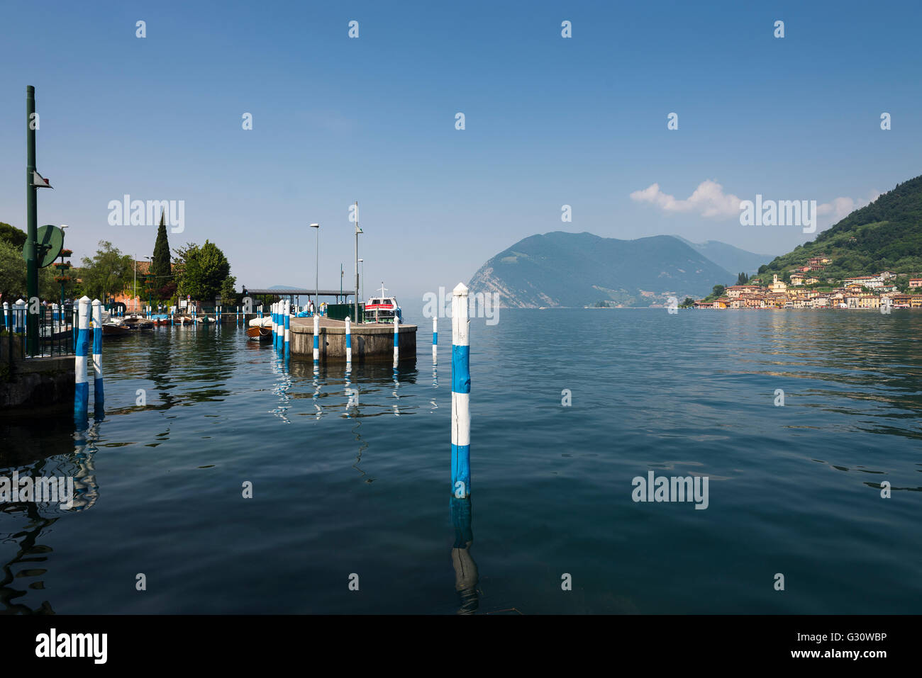 Colorful poles at the port of Sulzano on Lake Iseo with the panorama of ...