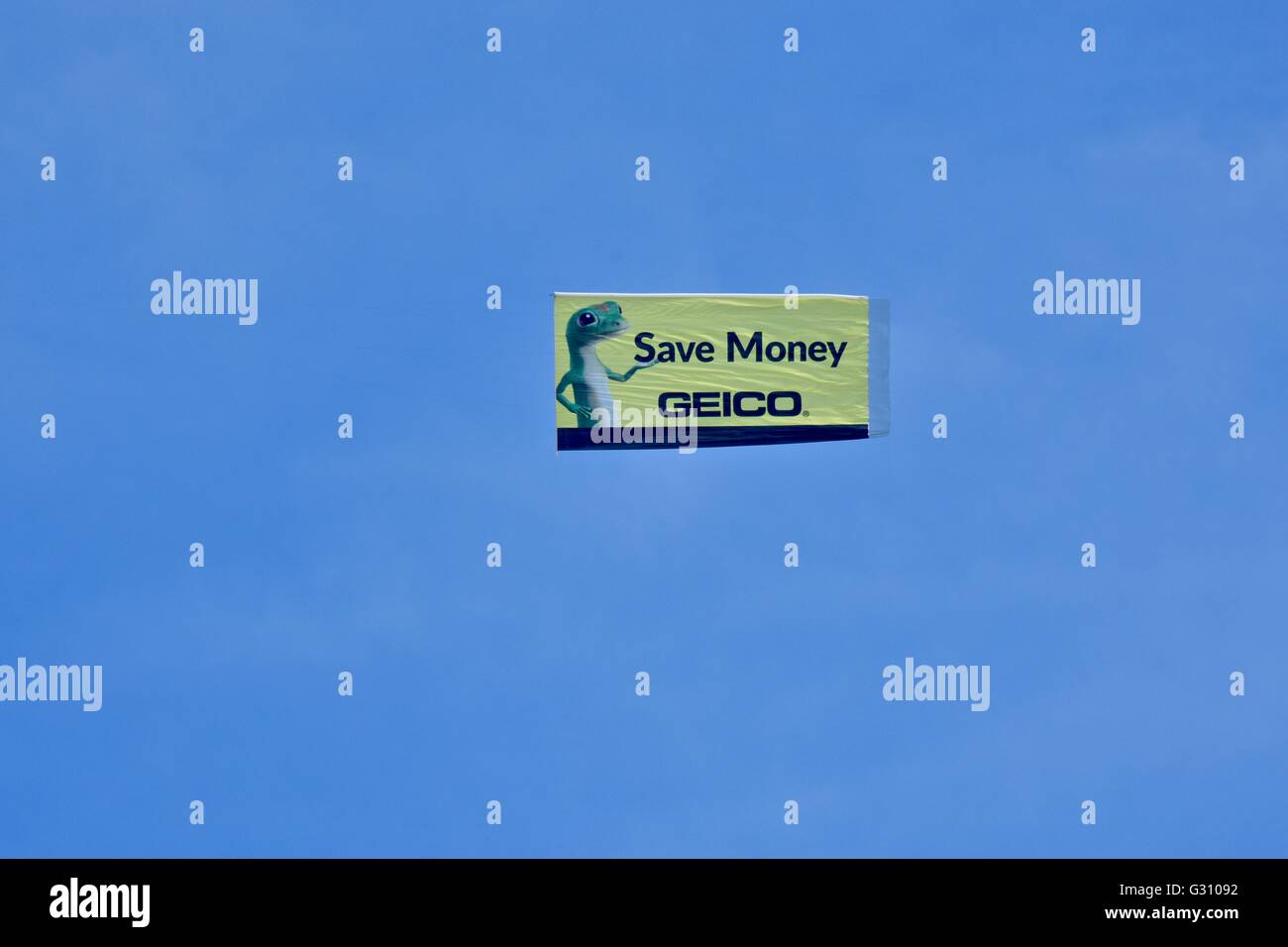 A small airplane pulling a Geico flag through the air on a blue sky ...