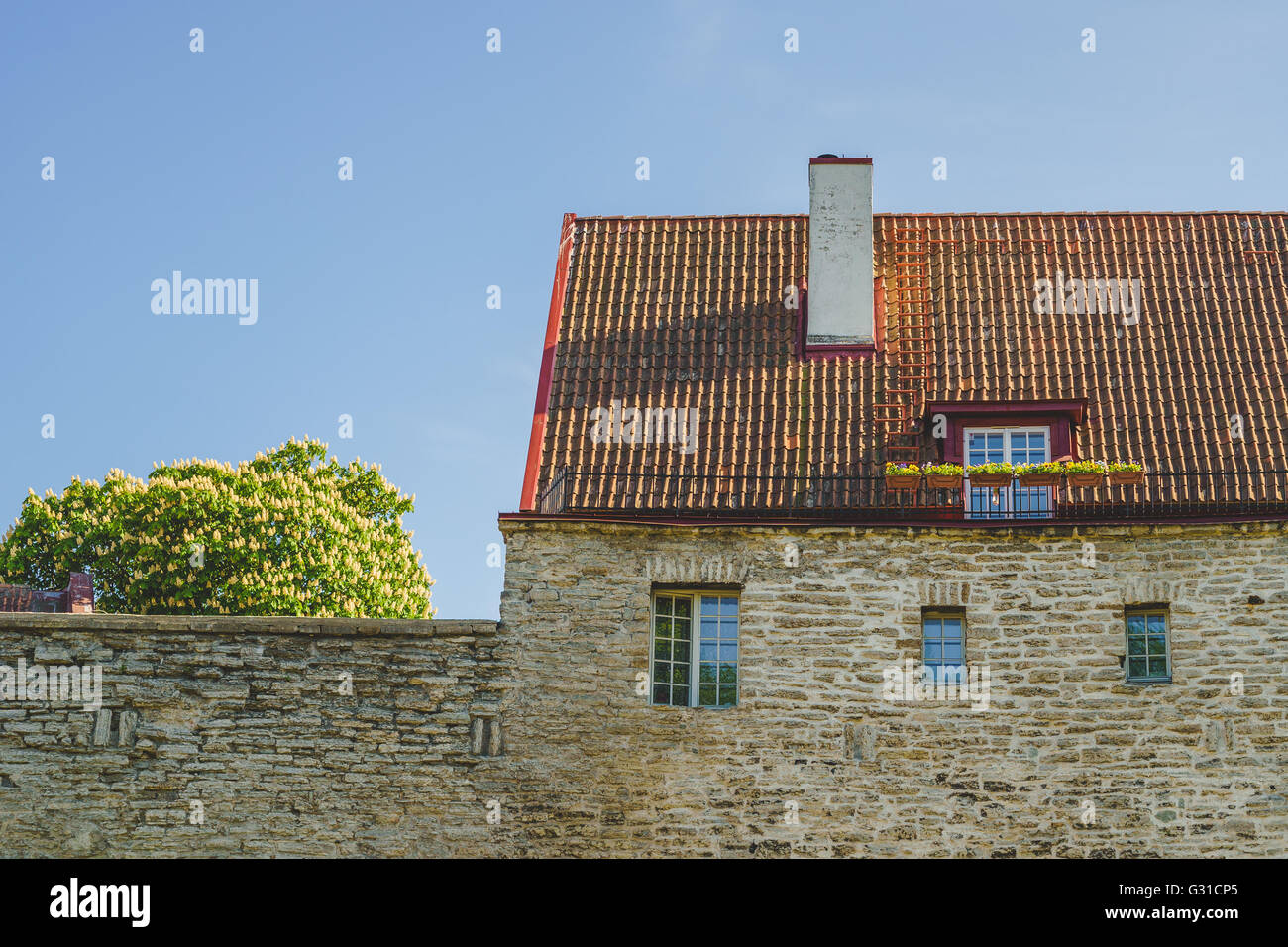 Medieval stone house facade. Red tile roof and mansard window with ...