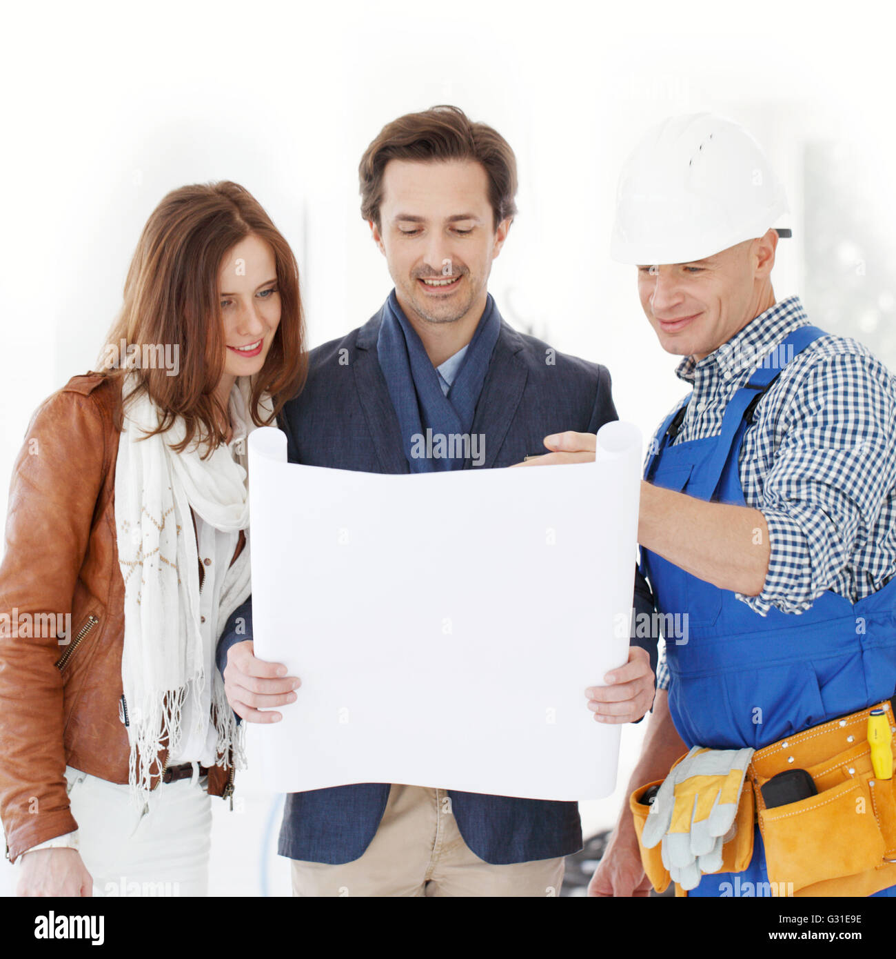 Worker shows house design plans to a young couple at construction site ...
