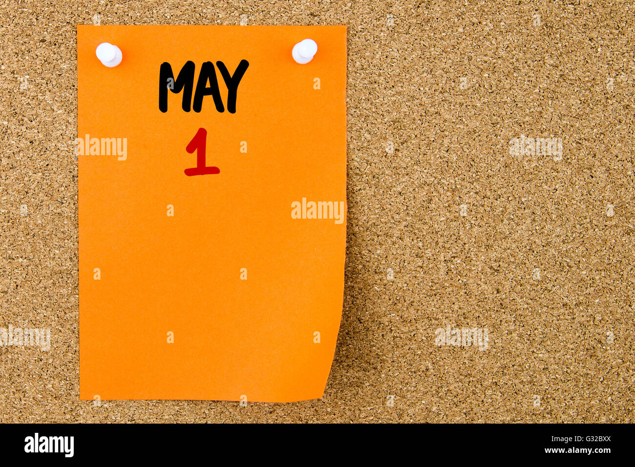 1 MAY written on orange paper note pinned on cork board with white ...