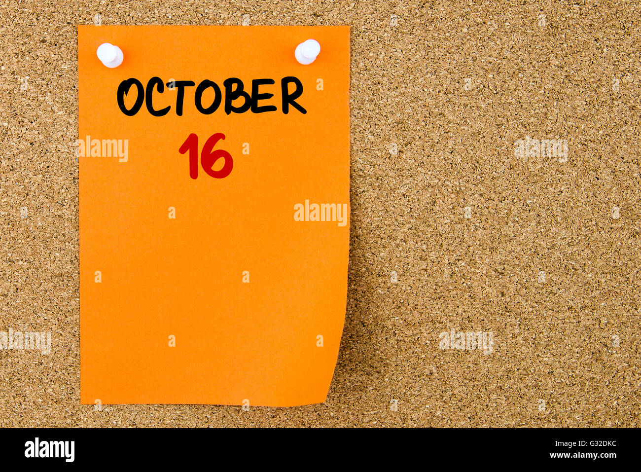 16 OCTOBER written on orange paper note pinned on cork board with white thumbtacks, copy space ...