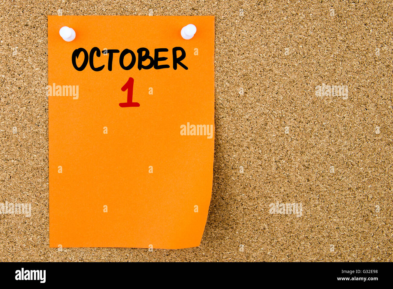 1 OCTOBER written on orange paper note pinned on cork board with white ...