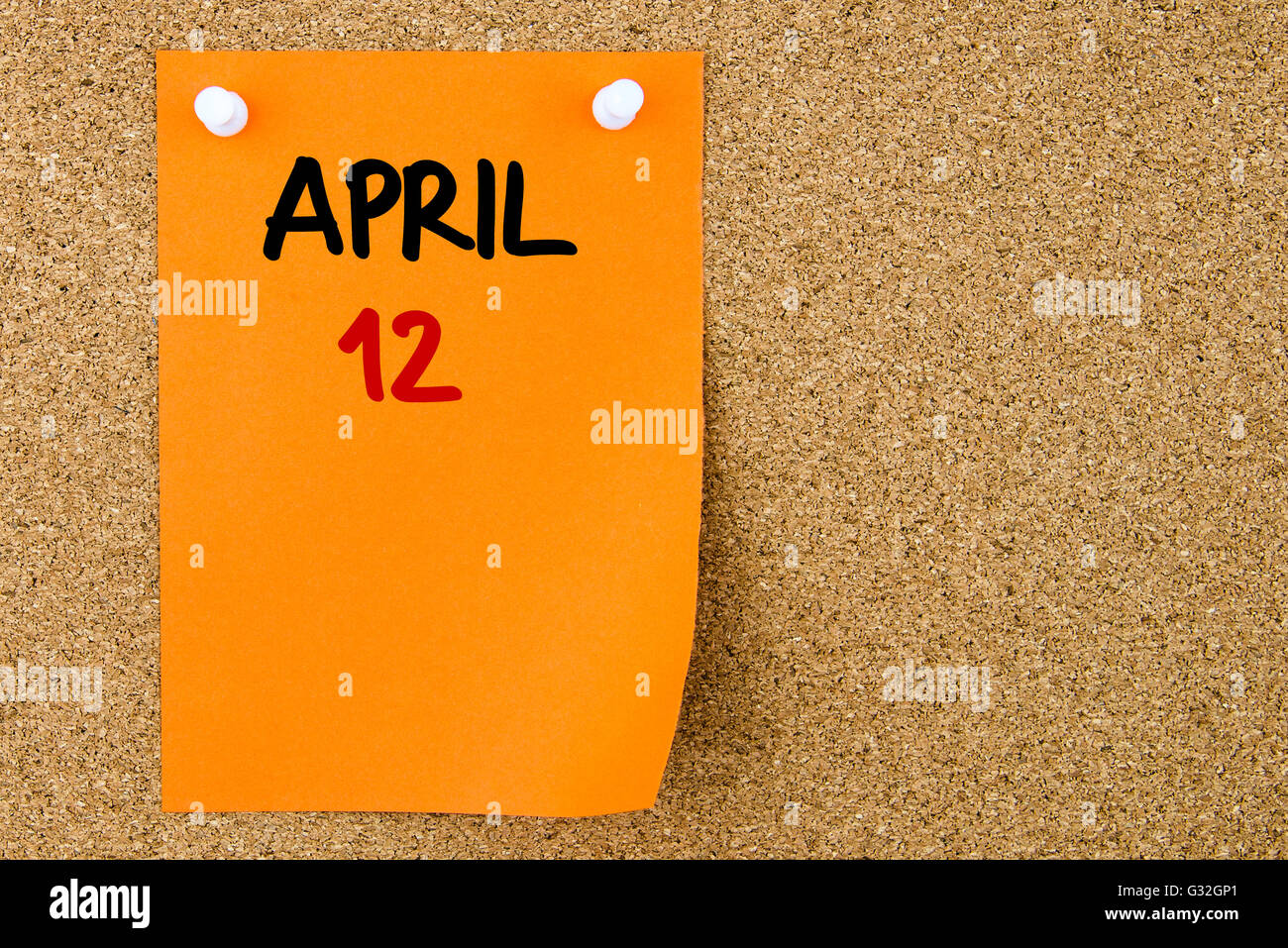 12 APRIL written on orange paper note pinned on cork board with white ...