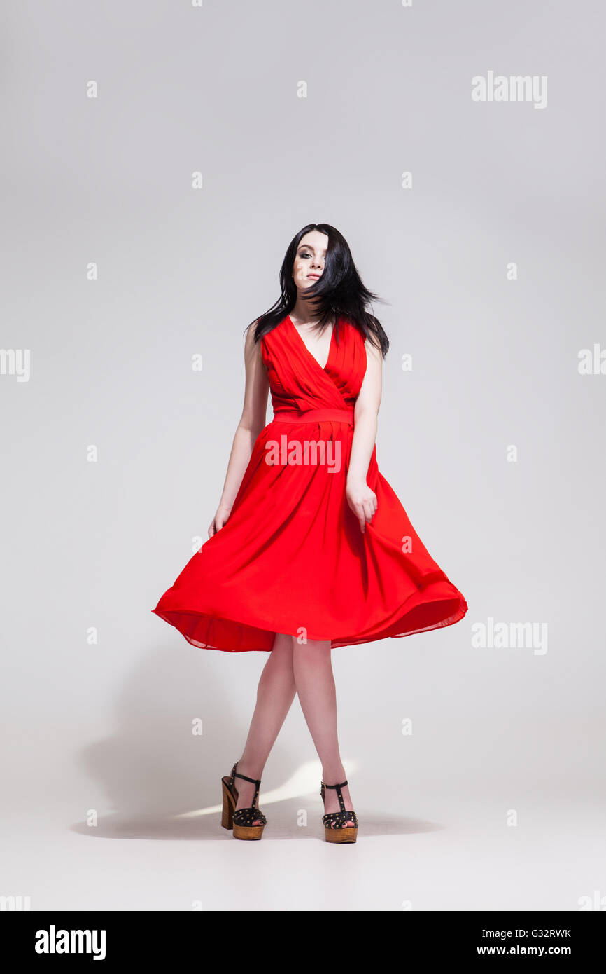 Portrait of beautiful young woman twisting in red dress while looking ...