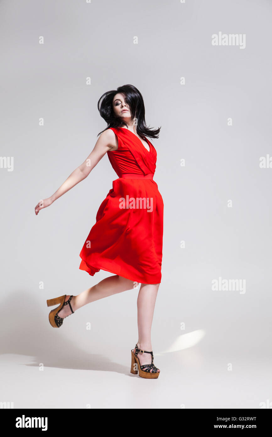 Portrait of beautiful young woman twisting in red dress while looking ...