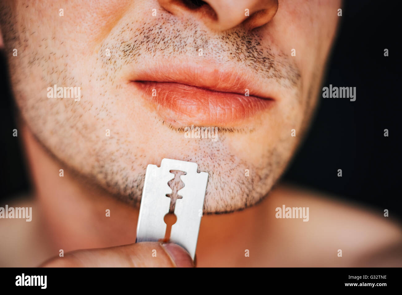 Man holding razor blade against chin Stock Photo - Alamy