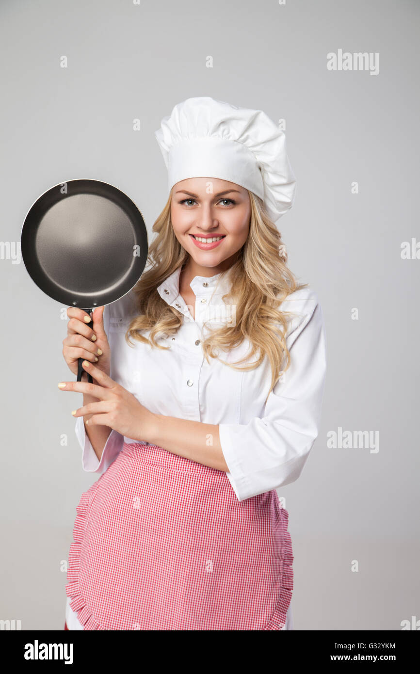 Studio shot of beautiful smiling woman in apron and hat showing frying ...