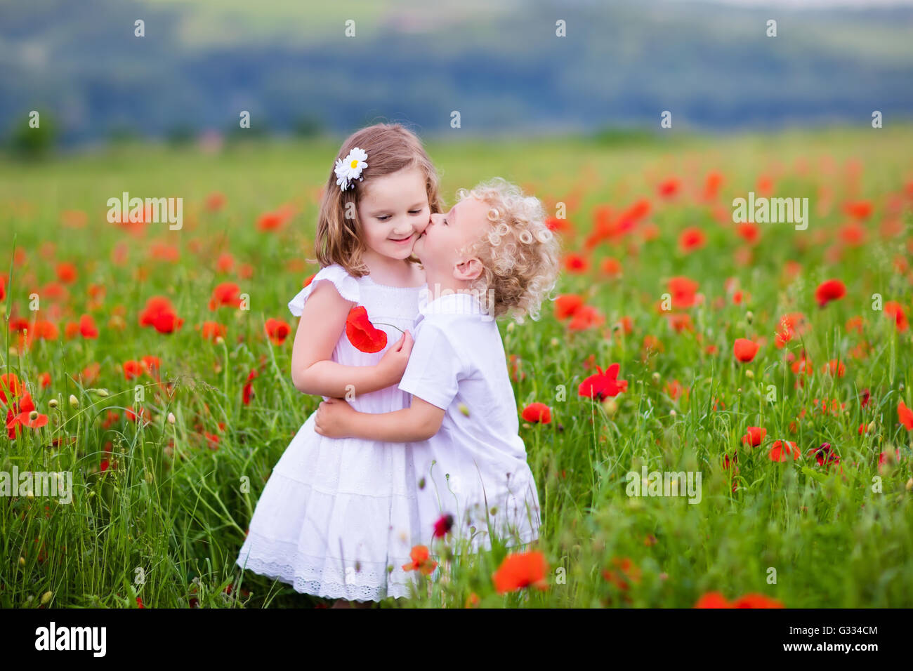 Little curly blond boy and girl play in poppy flower field. Child ...