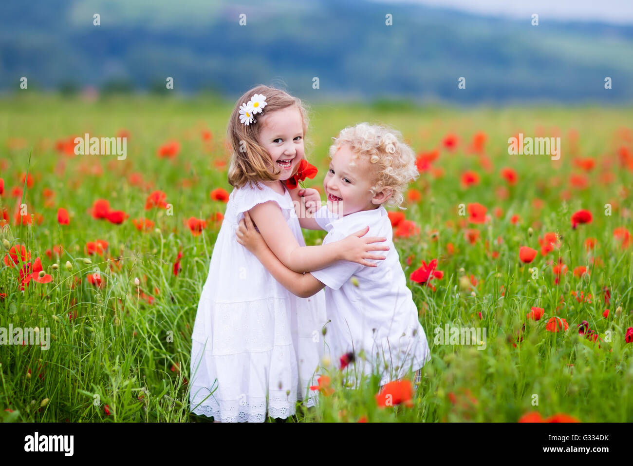 Little curly blond boy and girl play in poppy flower field. Child ...