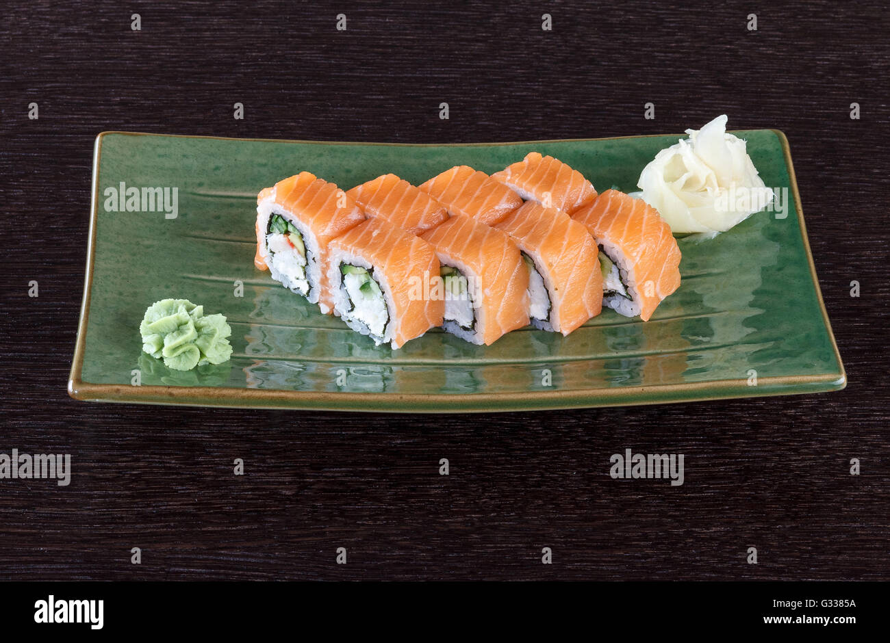 Sushi rolls on a plate with salmon on dark brown wooden table. Side ...