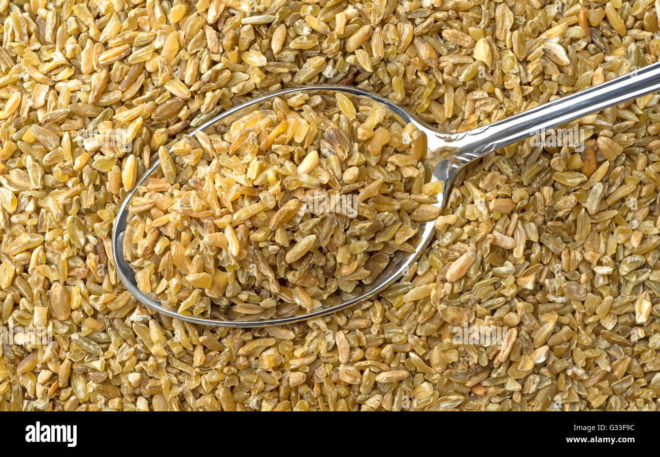 A very close view of cracked freekeh grain on a spoon with more wheat ...
