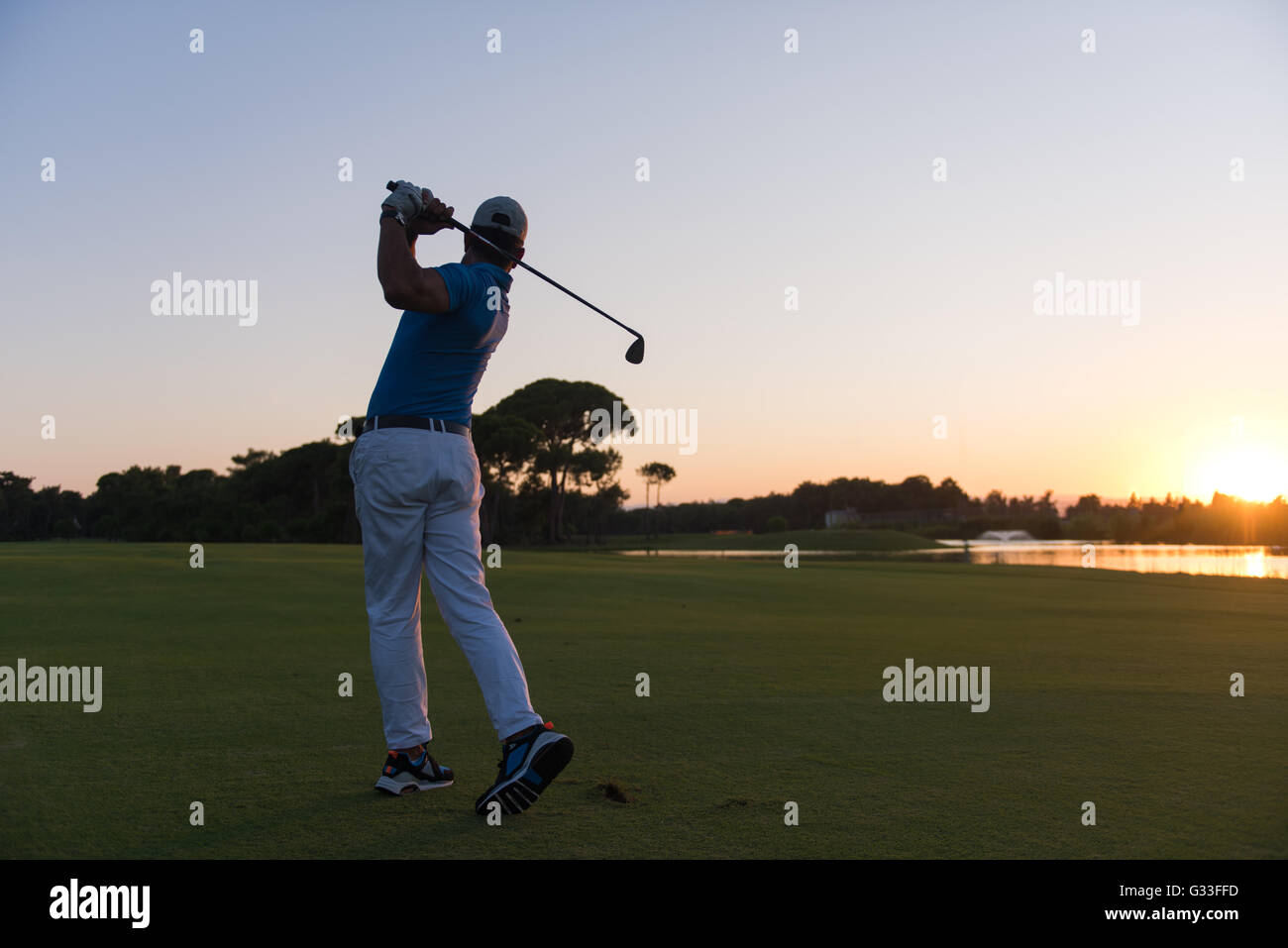 golfer hitting long shot with driver on course at beautiful sunset ...