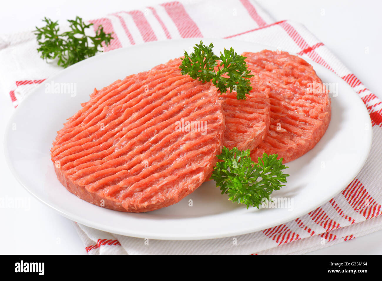 plate of raw hamburger patties on checkered dishtowel - close up Stock ...