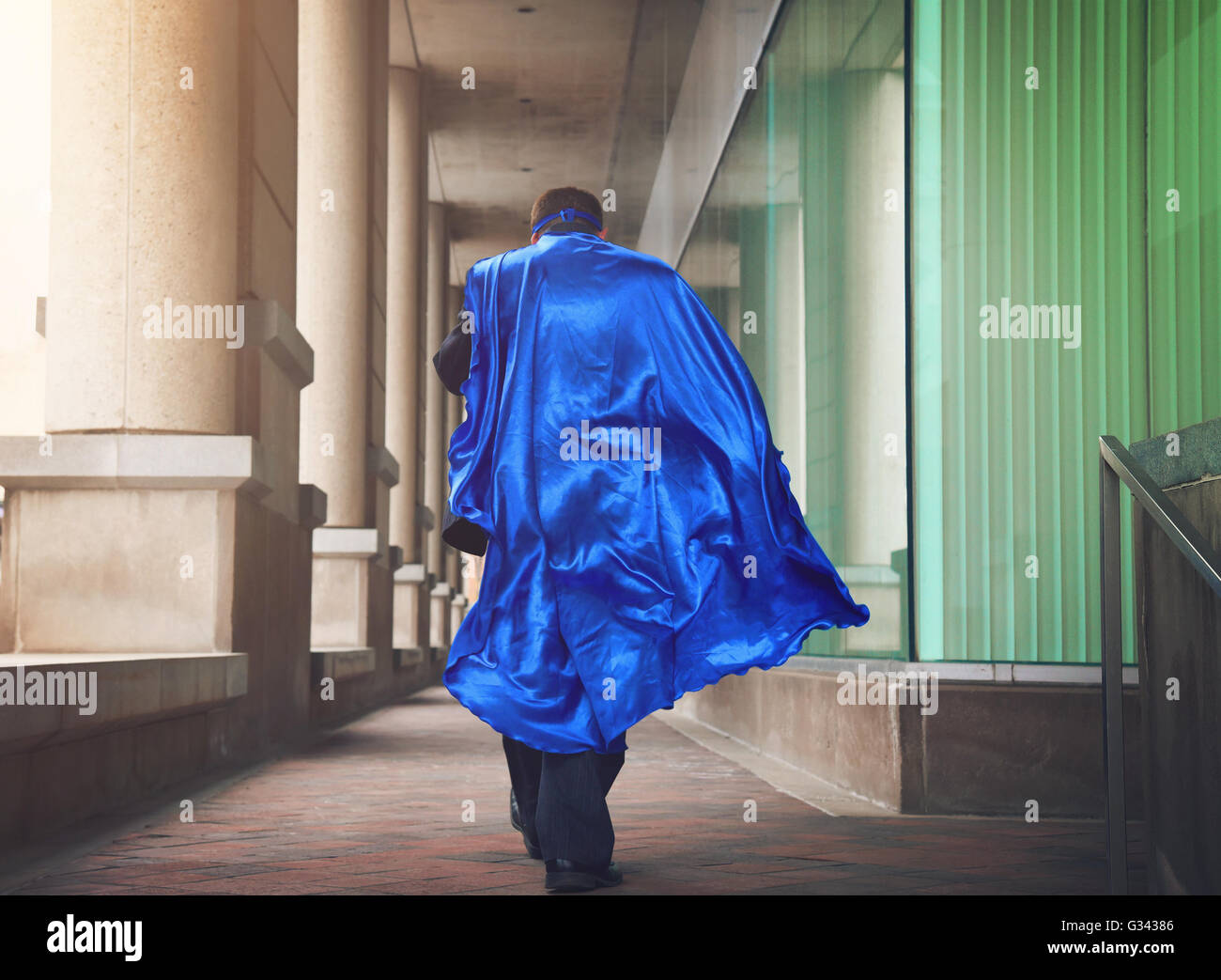 A business man is dressed as a super hero with a blue cape running in ...
