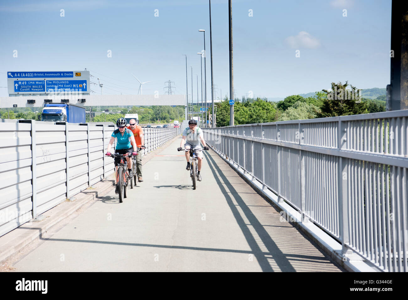 Three cyclists all wearing cycle helmets riding their bikes over the M5 ...
