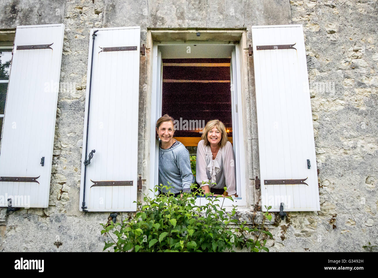 Two happy women looking out of shuttered window Stock Photo - Alamy