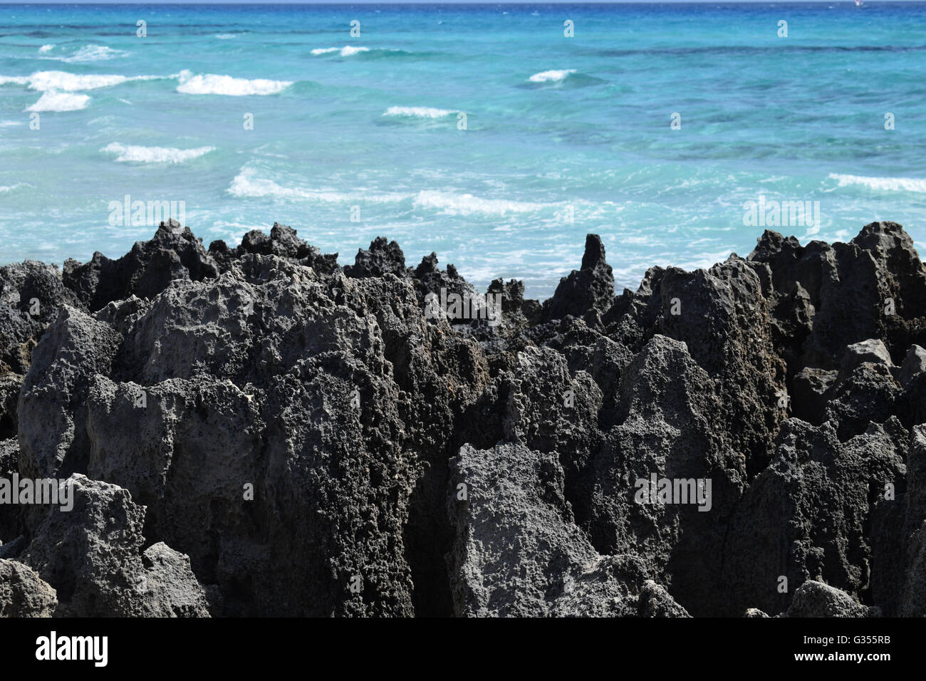 Volcanic rock formation against turquoise sea at Es Arenals beach ...