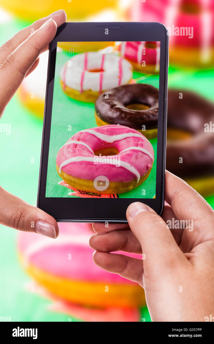 a woman using a smart phone to take a photo of some colorful donuts ...