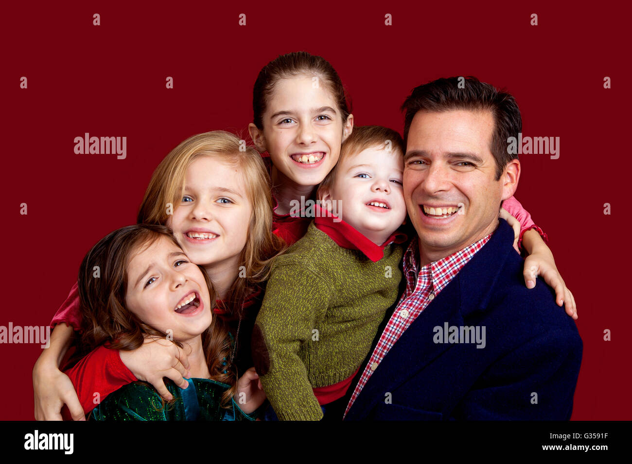 A good looking father poses with his four kids on a red background ...