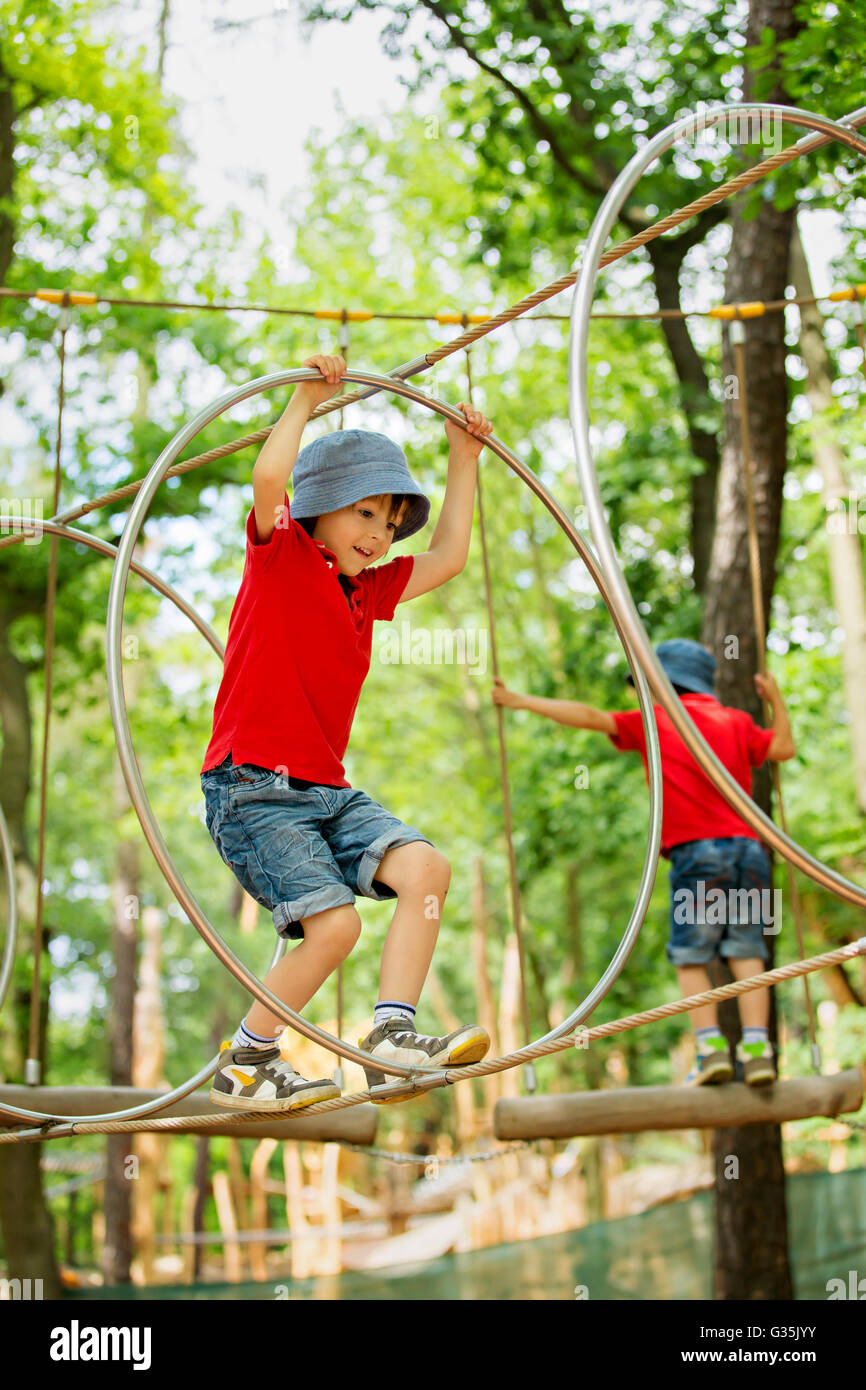 Two cute children, boy brothers, climbing in a rope playground ...