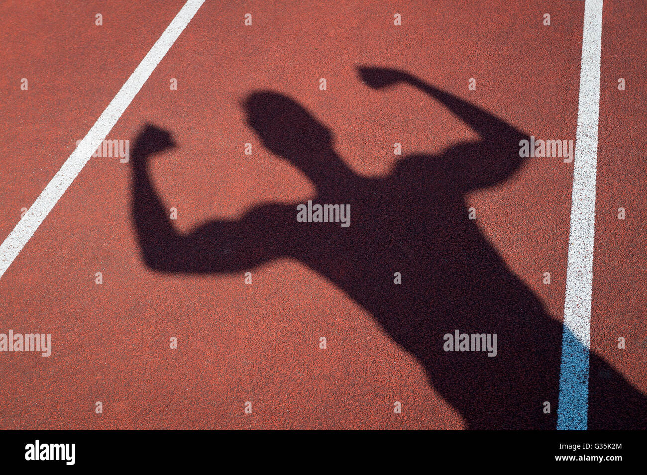 Athlete flexing his muscles casting a shadow on a bright red running ...