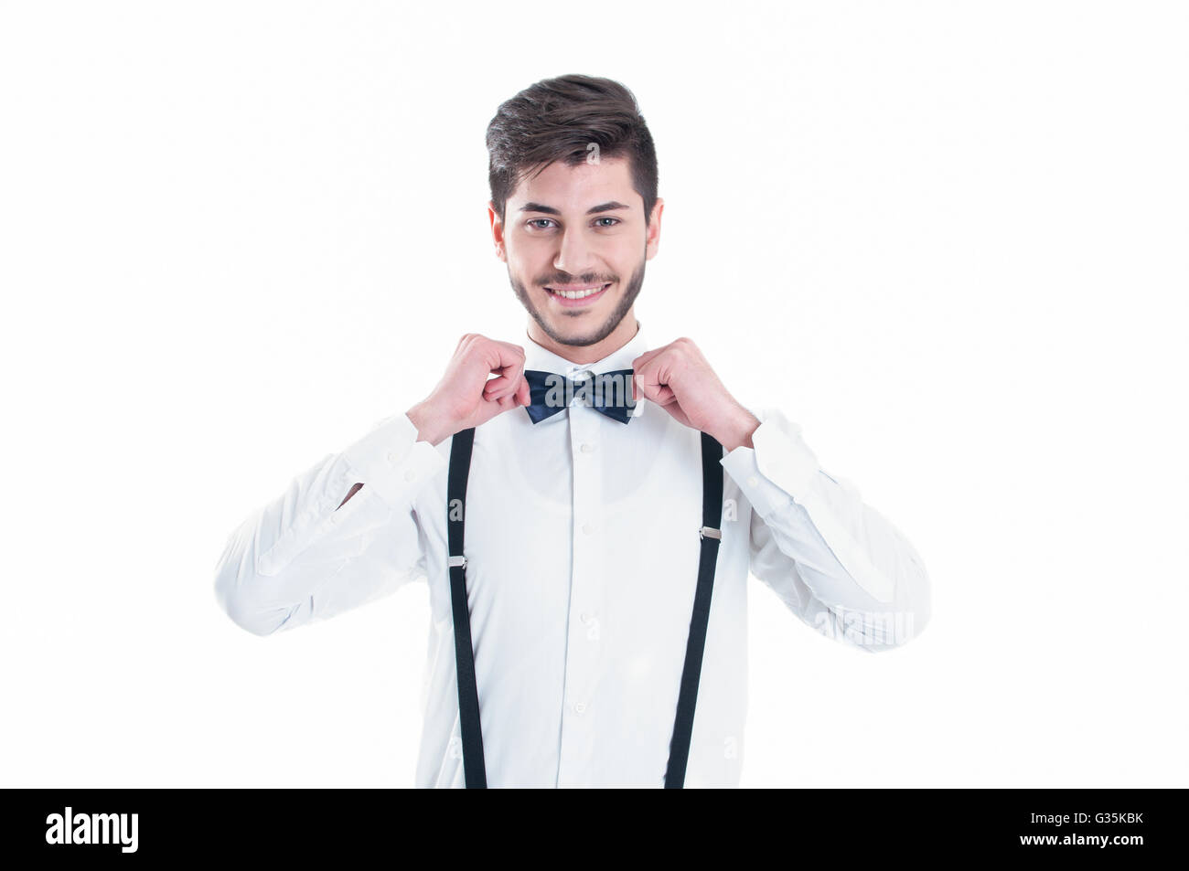Young man correcting his bow tie, smiling. Isolated on white background ...