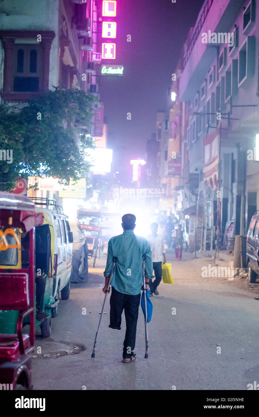 An Indian man with one leg on crutches walks down a slum in Delhi ...