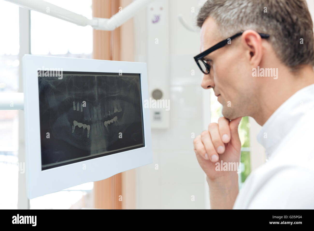 Male dentist looking teeth on digital X-Ray computer monitor wering ...