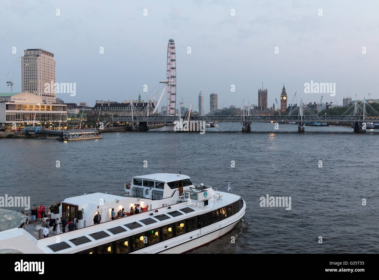 A cruiser sails up the River Thames as dusk falls, with Westminster in ...