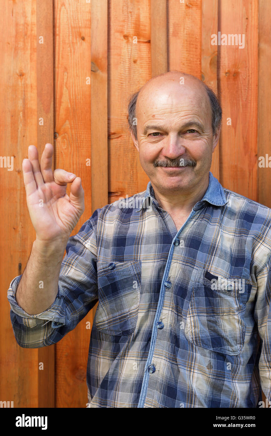 elderly man in a plaid shirt, bald, with a mustache shows sign okay ...