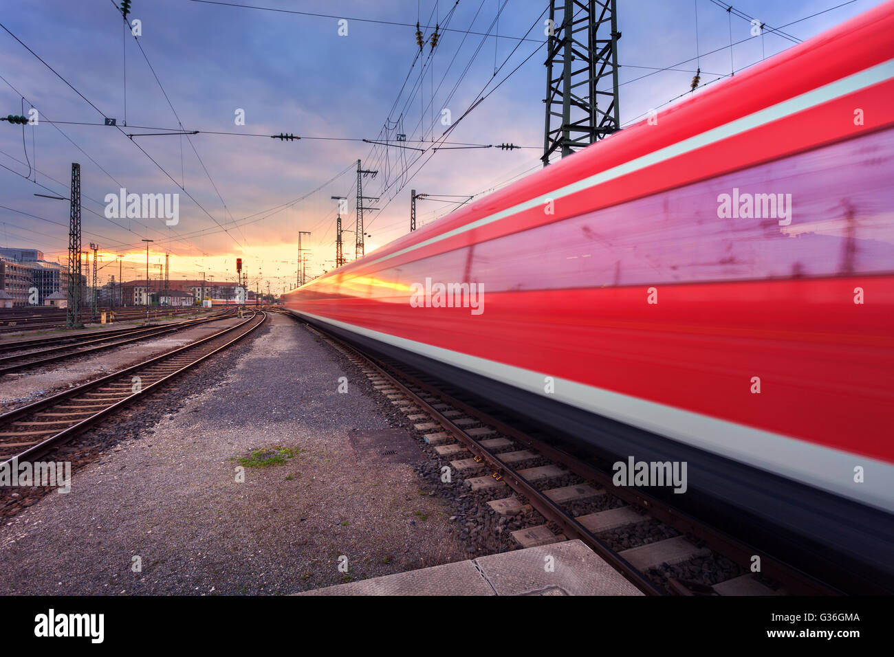 High speed red passenger train on railroad track in motion at sunset ...