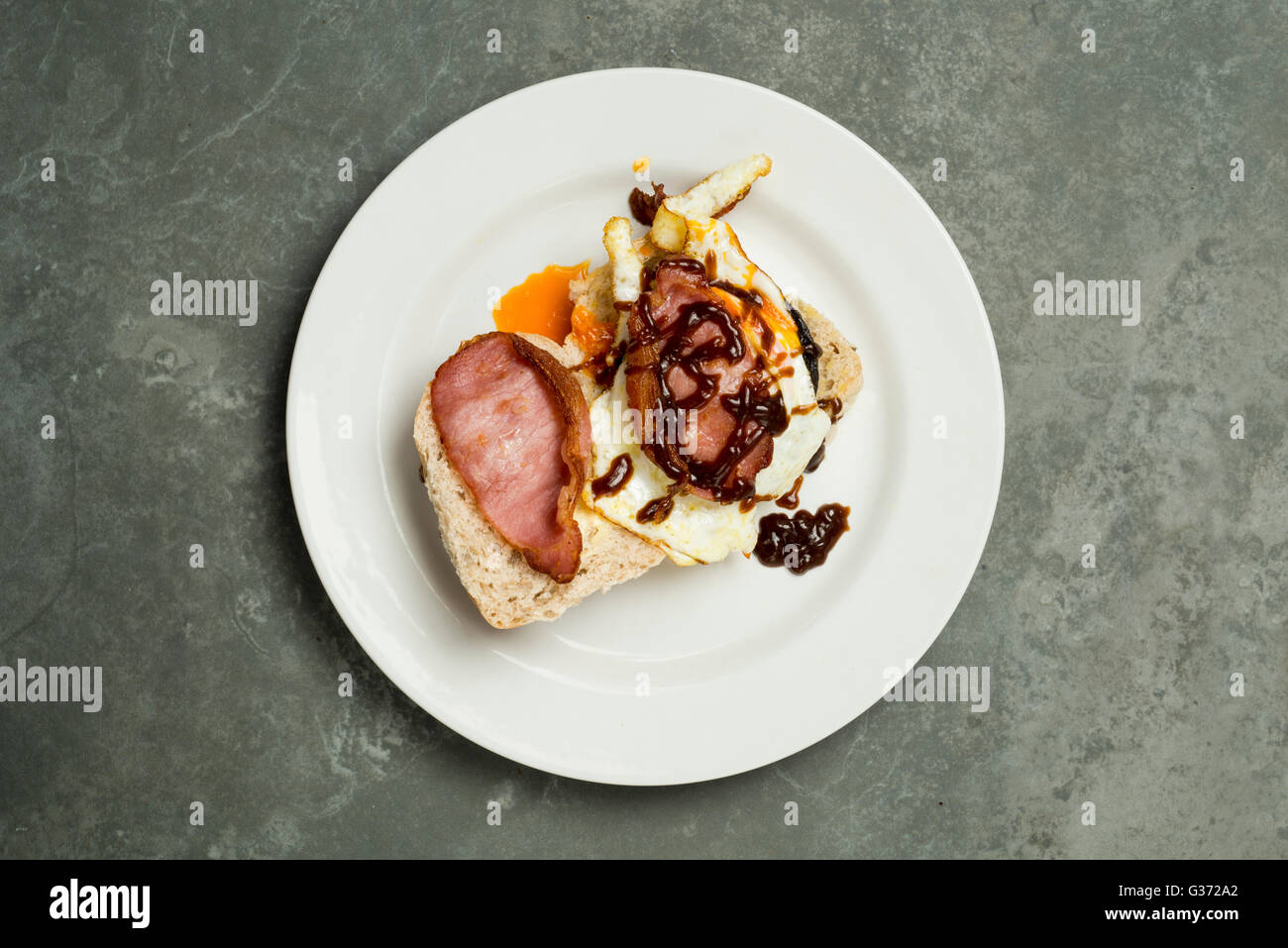 Overhead of bacon and egg on roll served on a white round plate Stock ...
