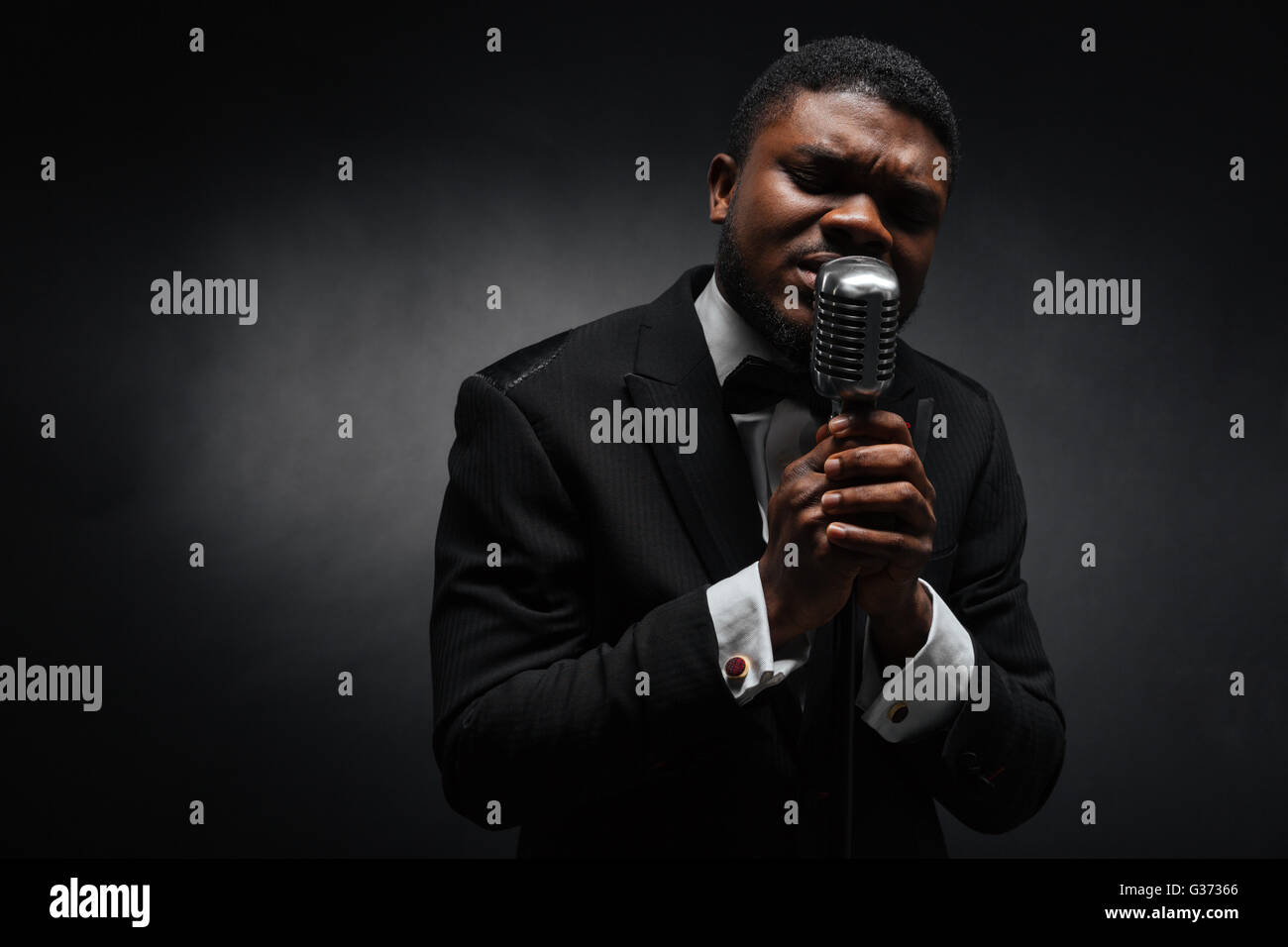 Handsome afro amerian man singing into vintage microphone over dark ...
