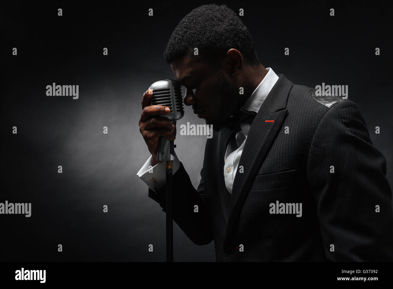 Afro amerian man singing into vintage microphone over dark background ...