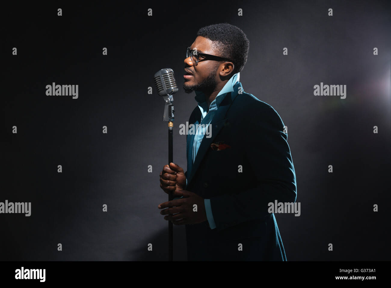 Afro amerian man singing into vintage microphone over dark background ...