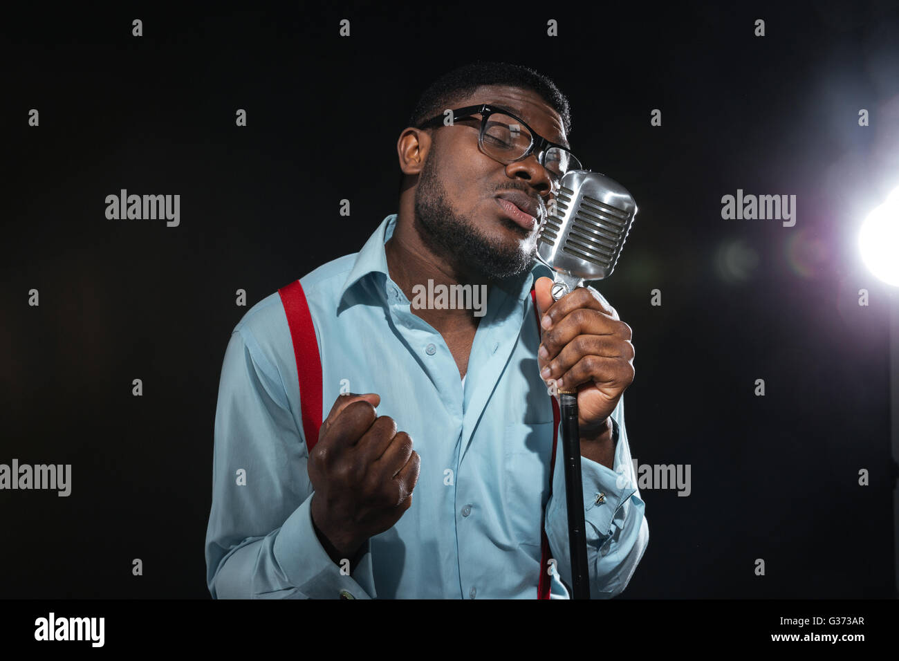 Handsome afro amerian man singing into vintage microphone over dark ...