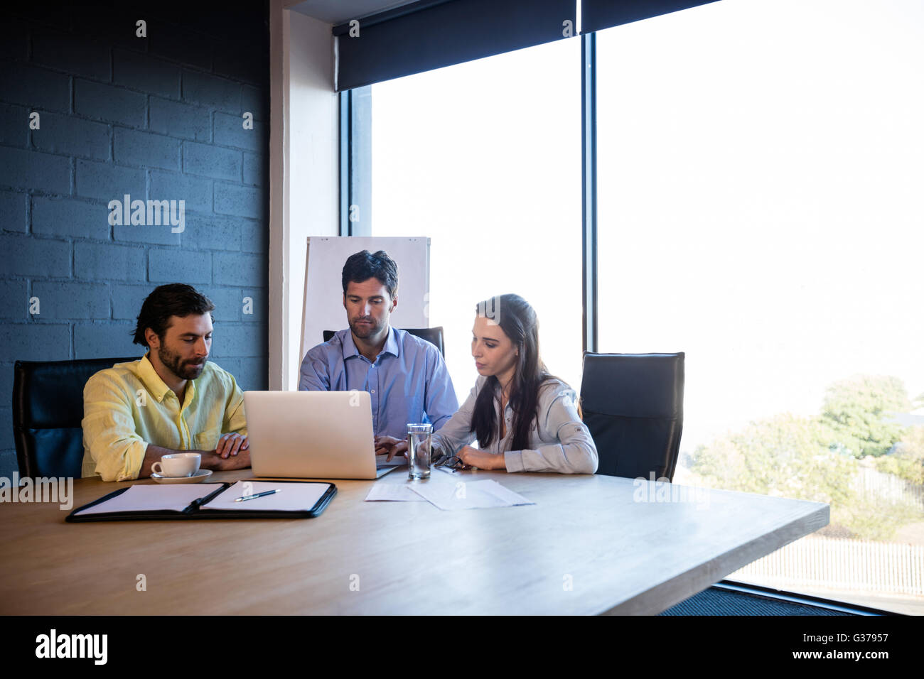 Coworkers working around a table with a laptop Stock Photo - Alamy