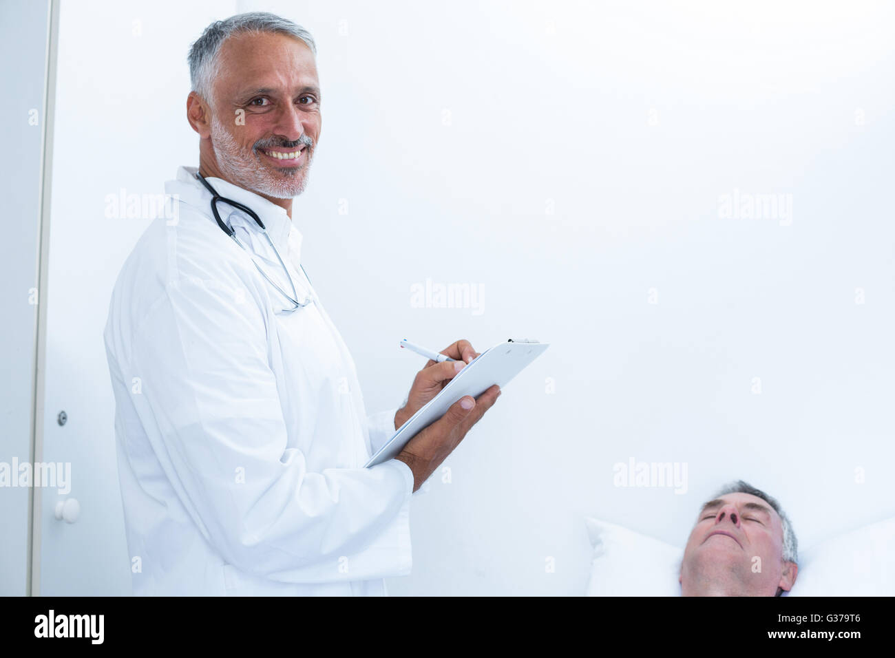 Male doctor writing medical report of senior man on clipboard Stock ...