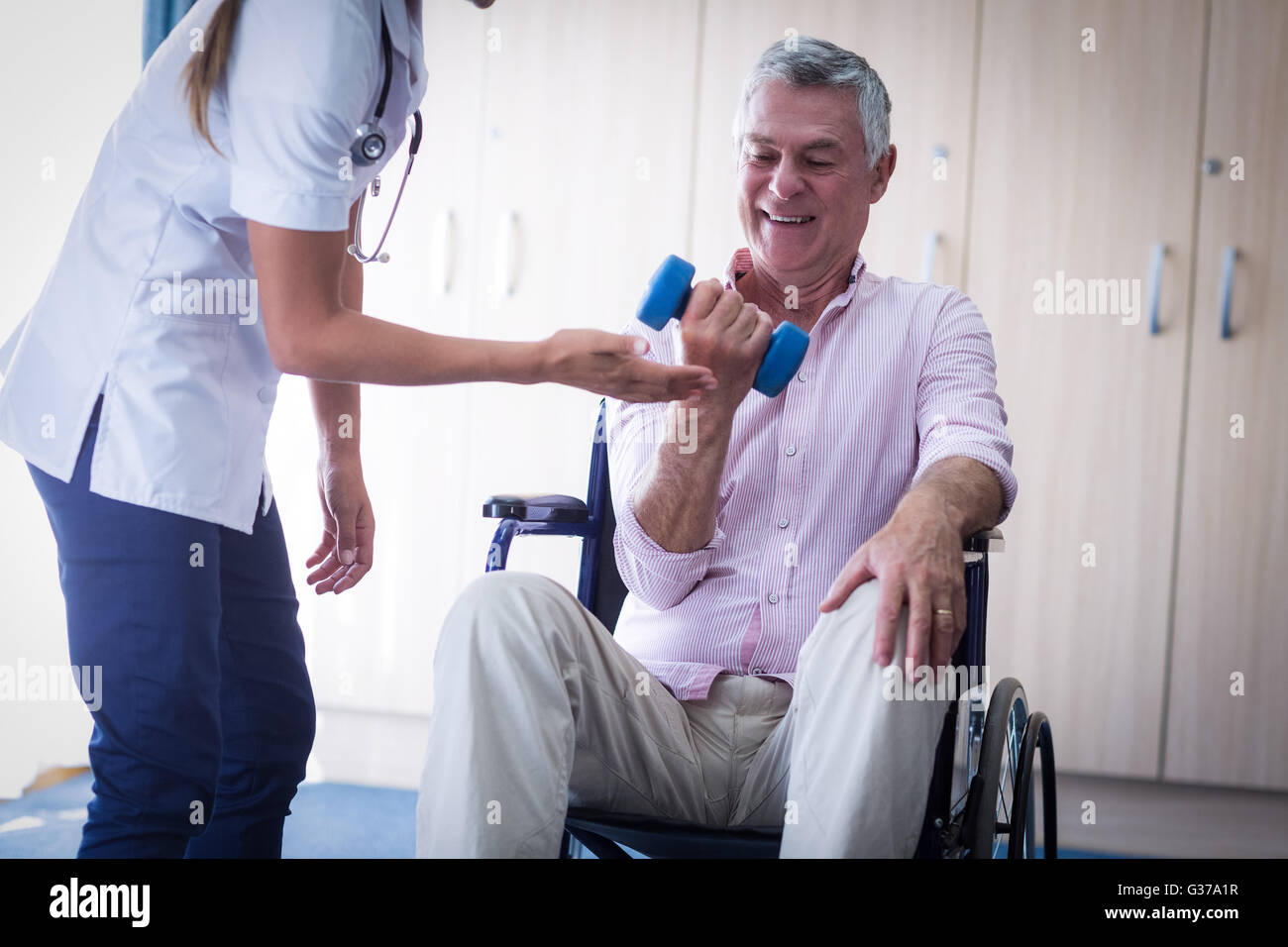 Female doctor assisting senior man in lifting dumbbell Stock Photo - Alamy