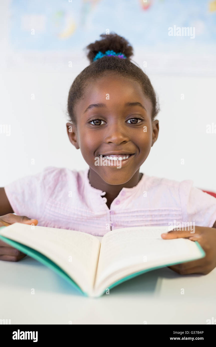 Smiling school girl reading book in classroom Stock Photo - Alamy