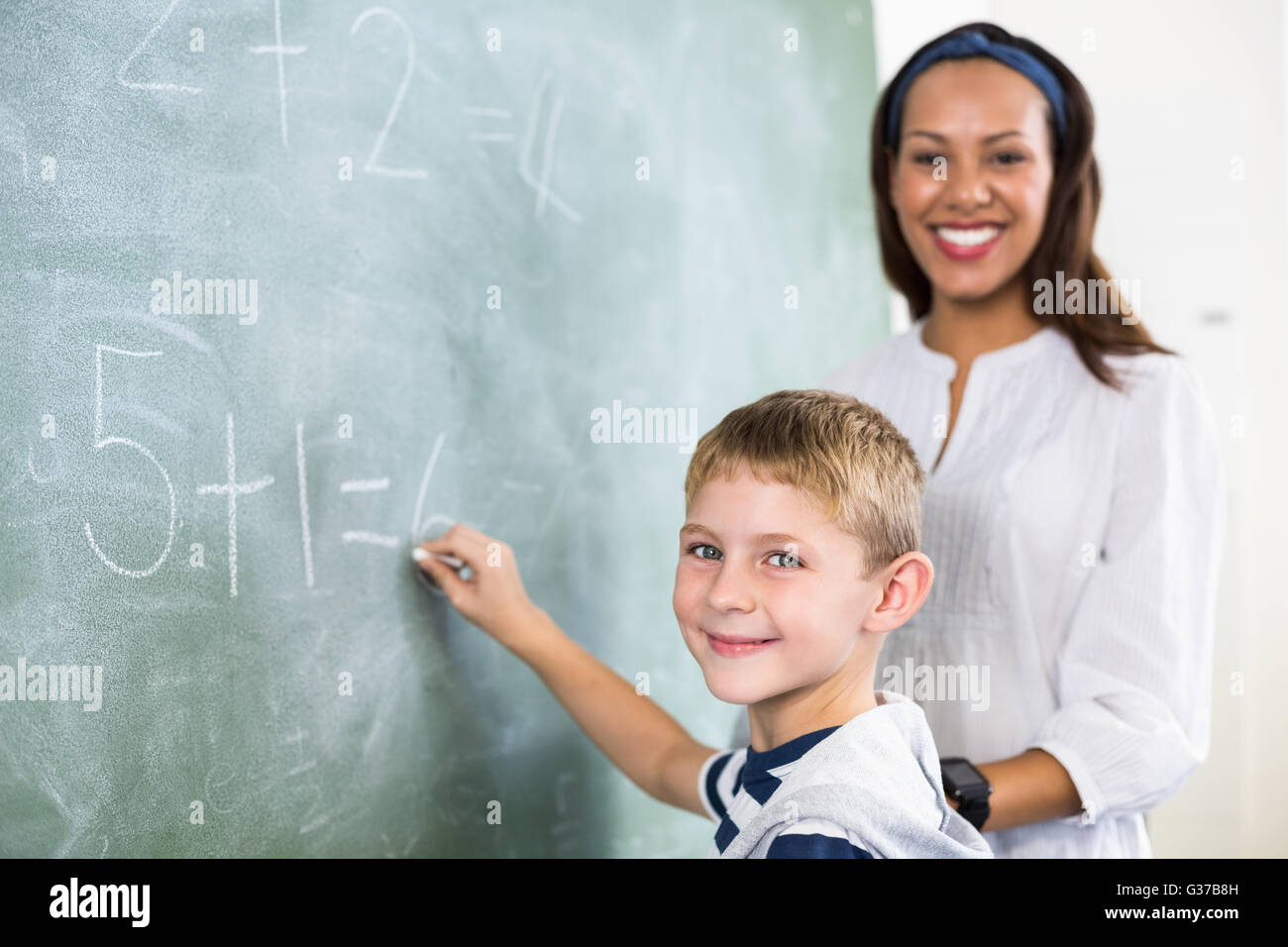 Portrait of teacher assisting boy in doing addition on chalkboard Stock ...