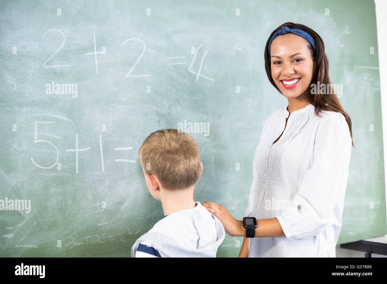 Smiling teacher assisting boy in doing addition on chalkboard Stock ...