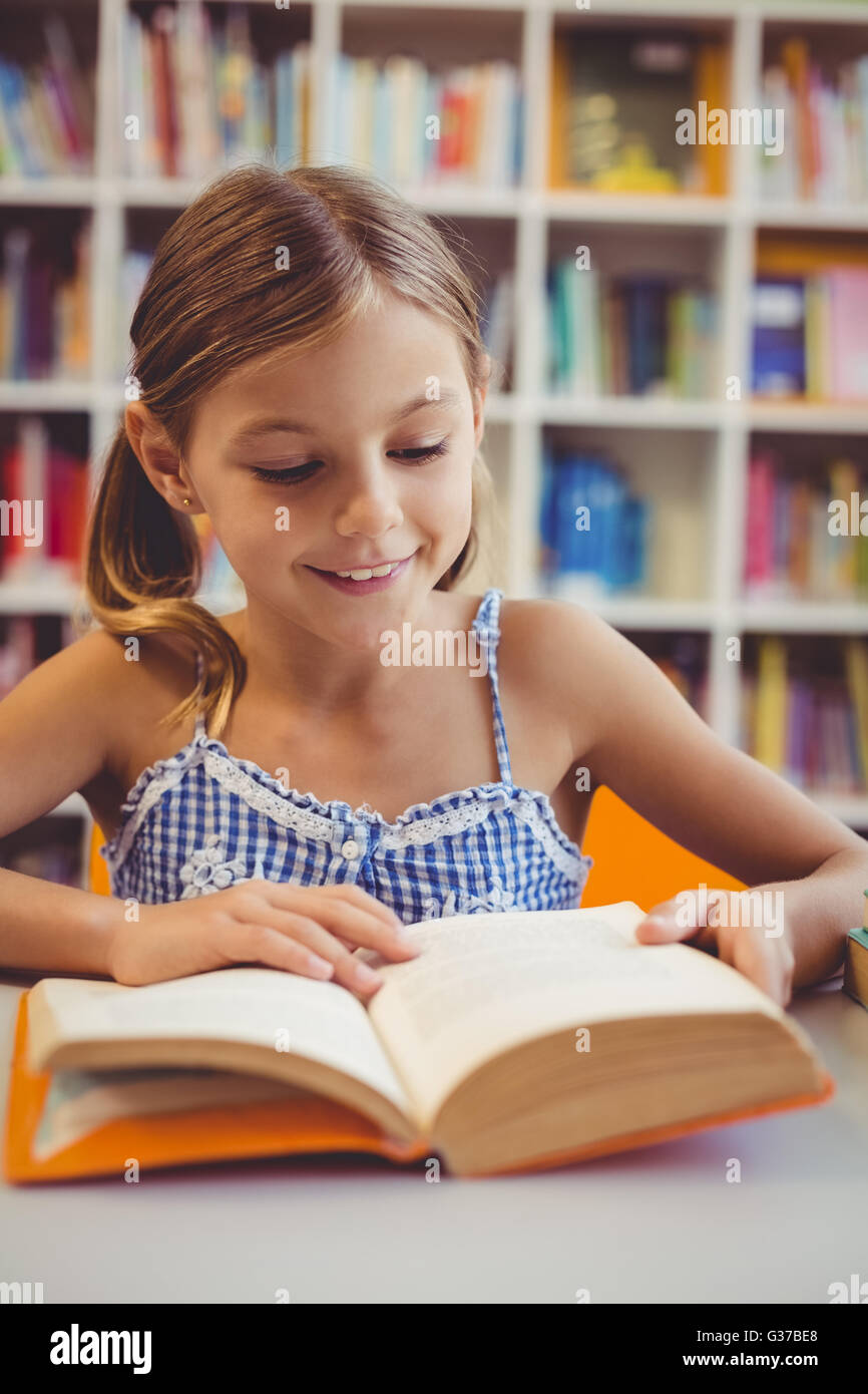 Smiling school girl reading a book in library Stock Photo - Alamy