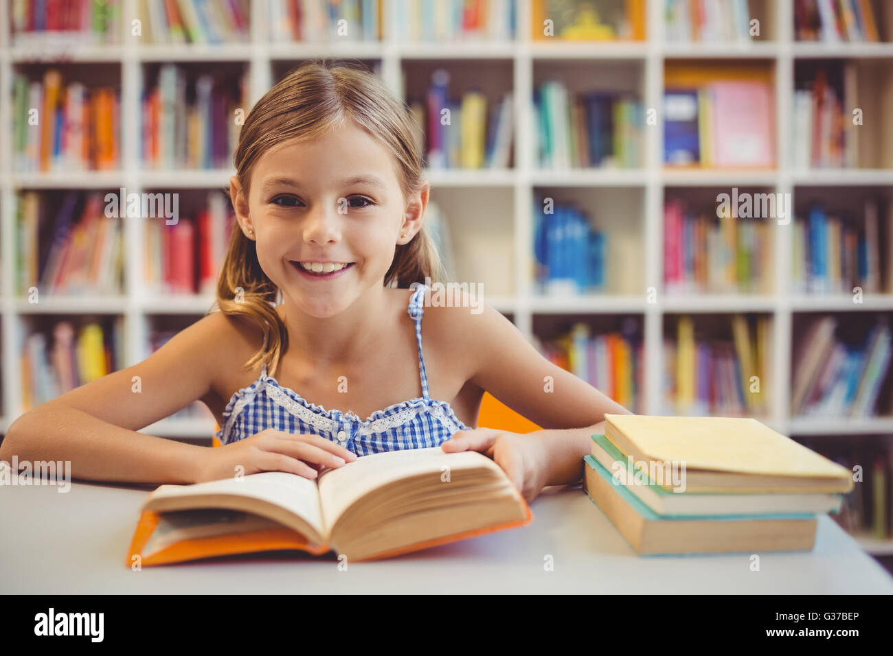 Smiling school girl reading a book in library Stock Photo - Alamy